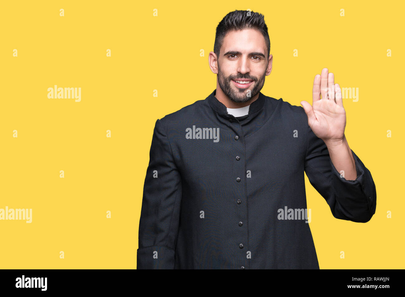 Young Christian priest over isolated background Waiving saying hello ...
