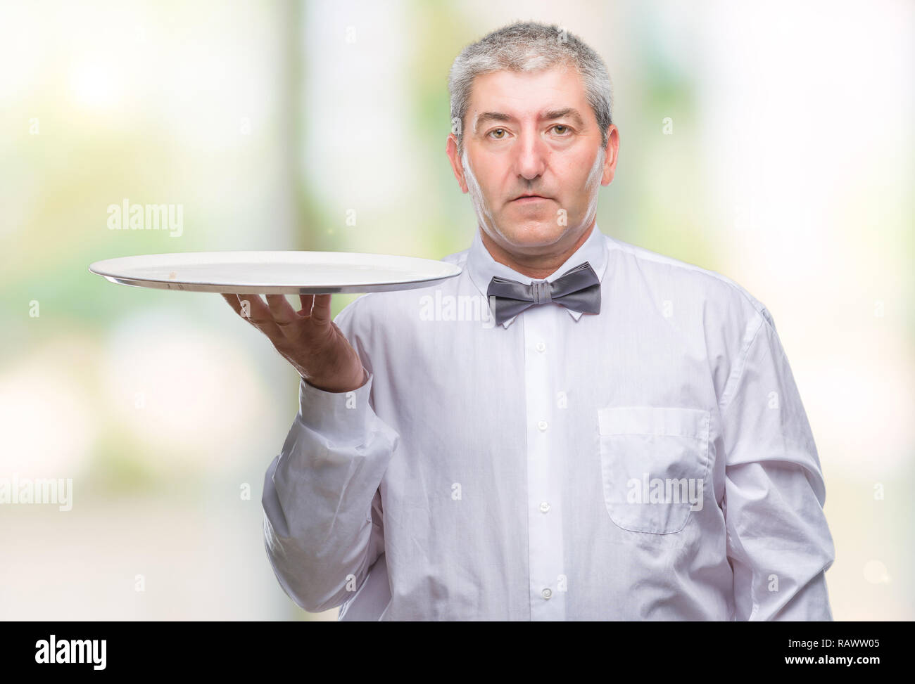 Handsome senior waiter man holding silver tray over isolated background ...