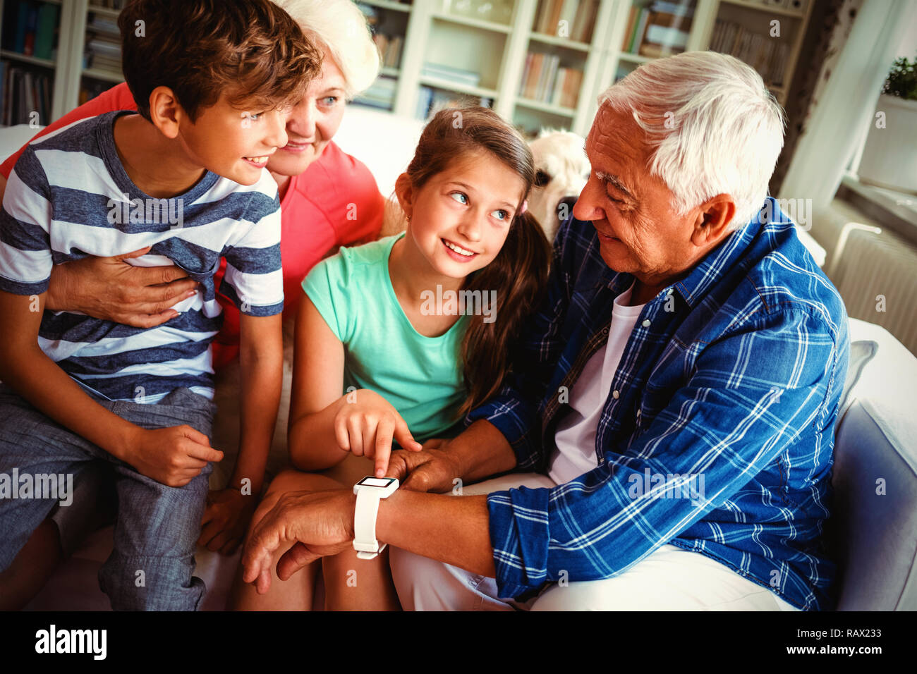 Grandparents and grandchildren looking at smartwatch in living room ...