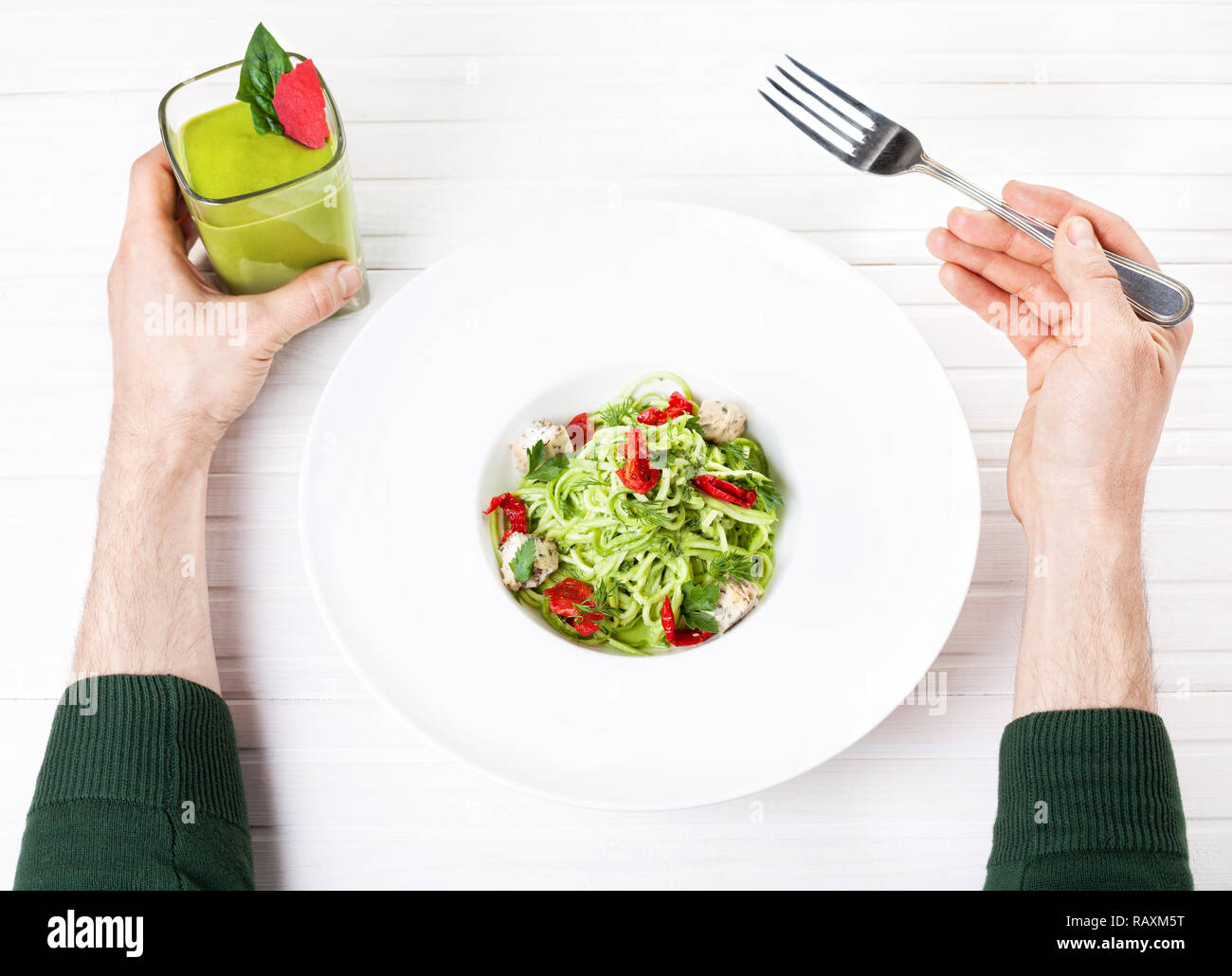 Man holding green smoothie and eating Raw vegan spaghetti from zucchini ...