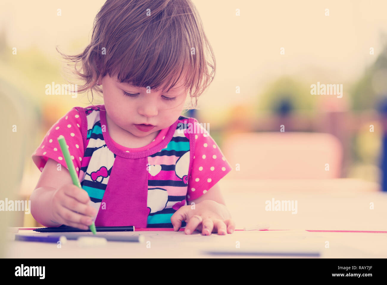 cute little girl cheerfully spending time using pencil crayons while ...