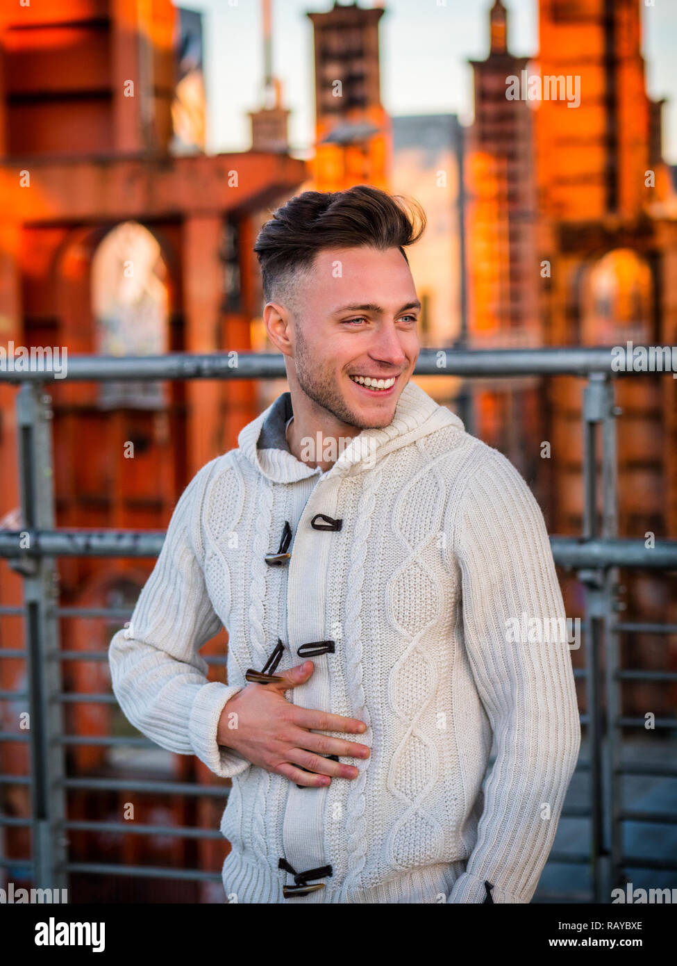Handsome trendy young man smiling and laughing, standing on a sidewalk ...