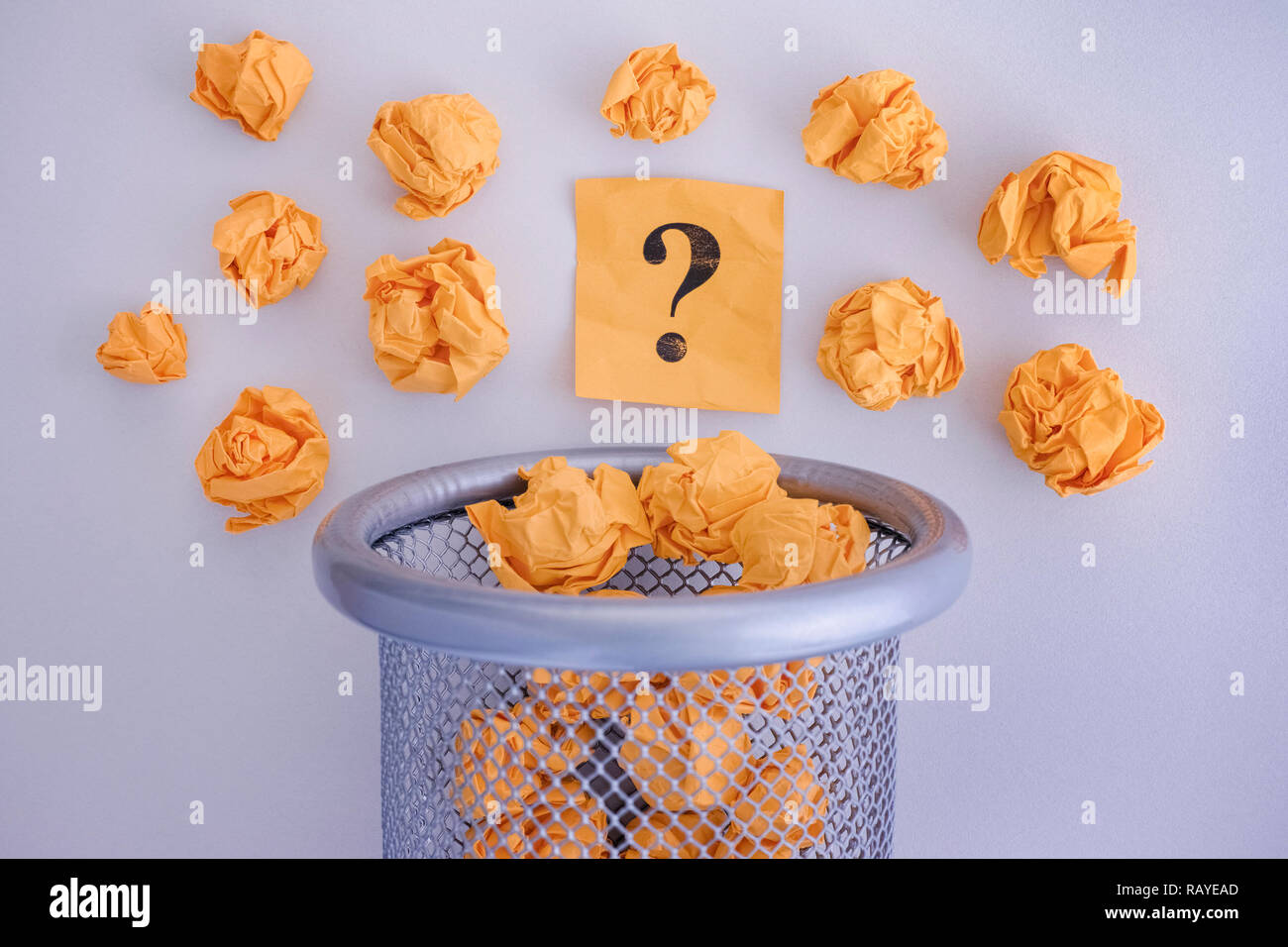 Yellow crumpled paper balls and question mark rolling out of a trash ...