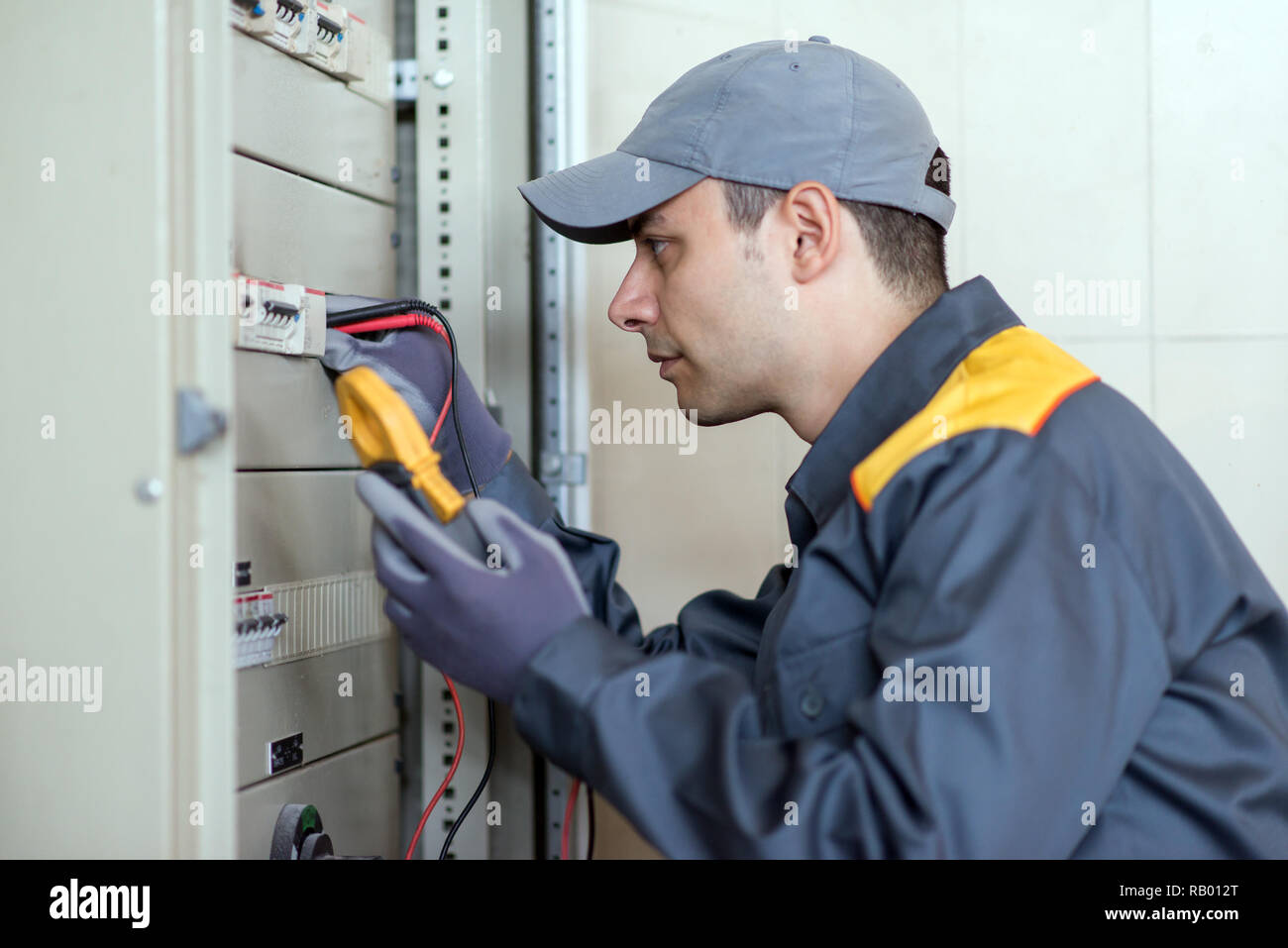 Electrician at work using a tester on an industrial panel in a factory ...