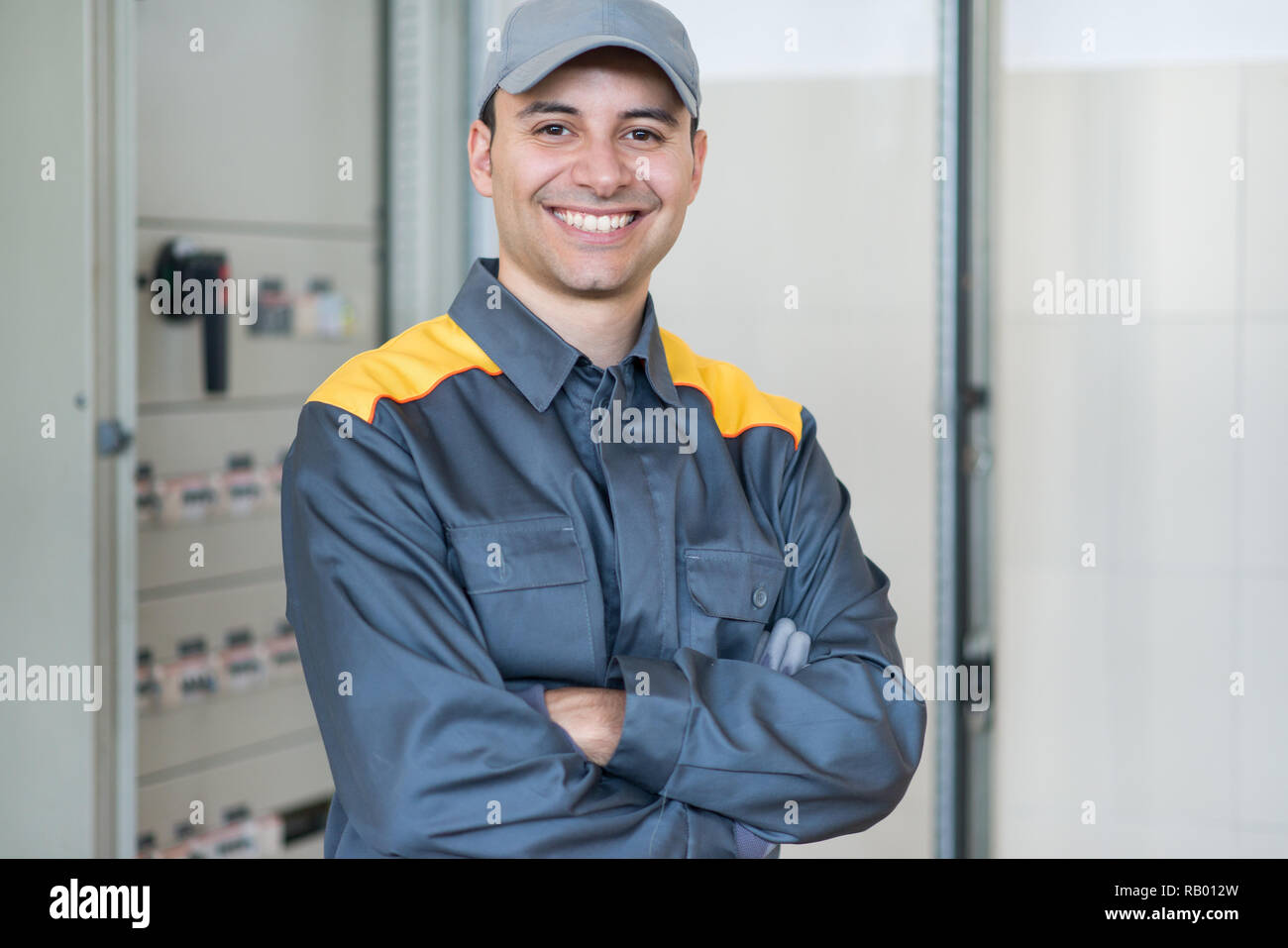 Portrait of a smiling electrician in front of an industrial electric ...