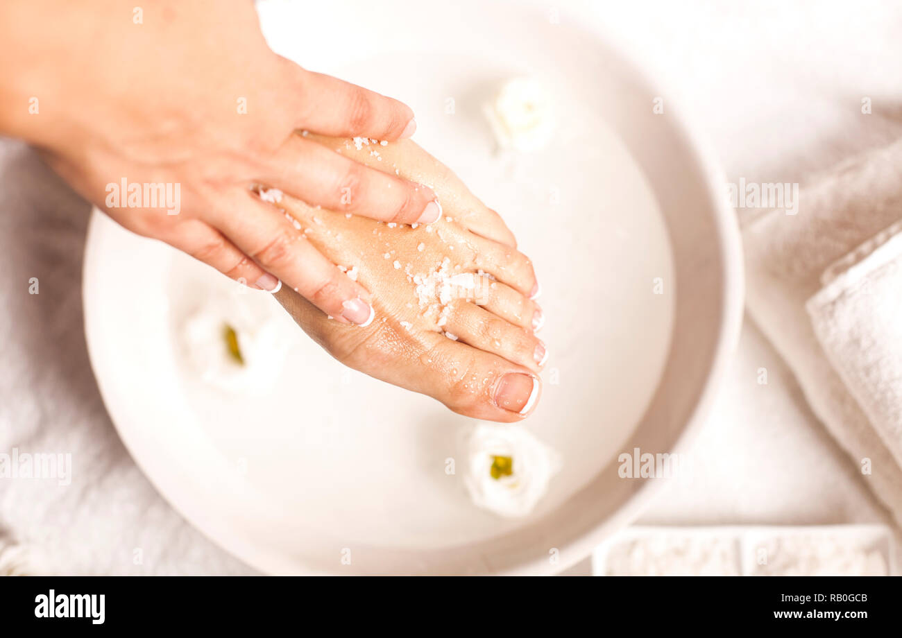 Female feet with sea salt soaked in a bowl of water on white background ...