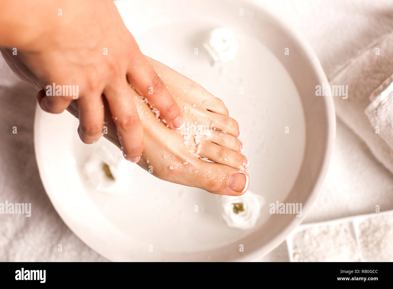 Female feet with sea salt soaked in a bowl of water on white background ...