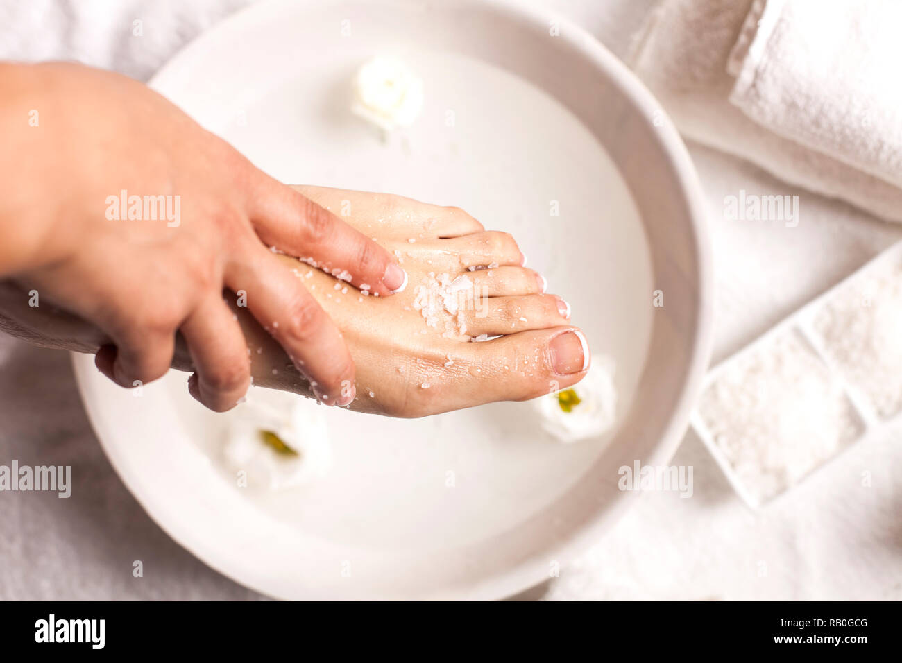 Female feet with sea salt soaked in a bowl of water on white background ...