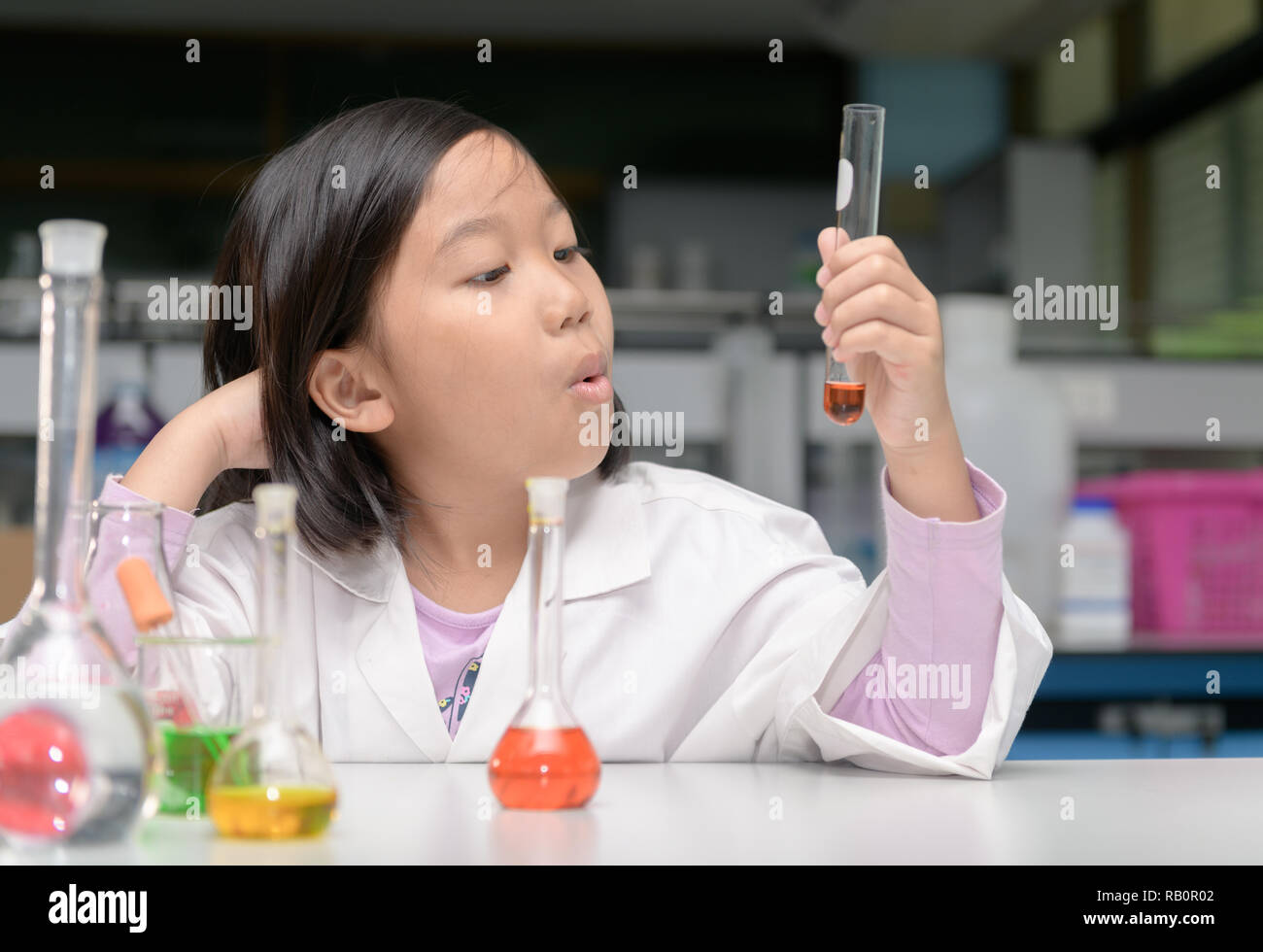 Happy little scientist in lab coat making experiment with test tube in ...