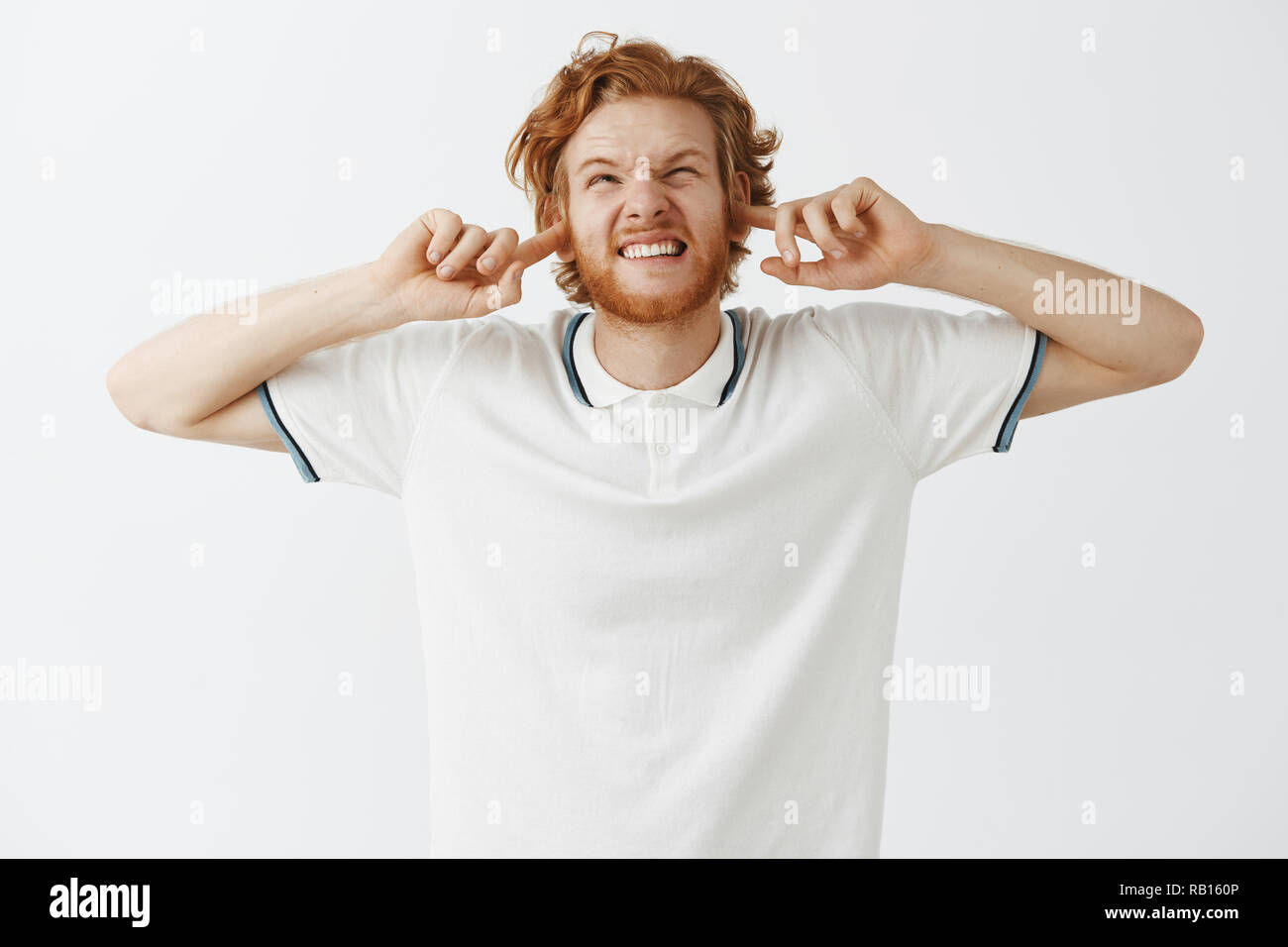 Bothered and annoyed redhead guy feeling discomfort of hearing loud ...