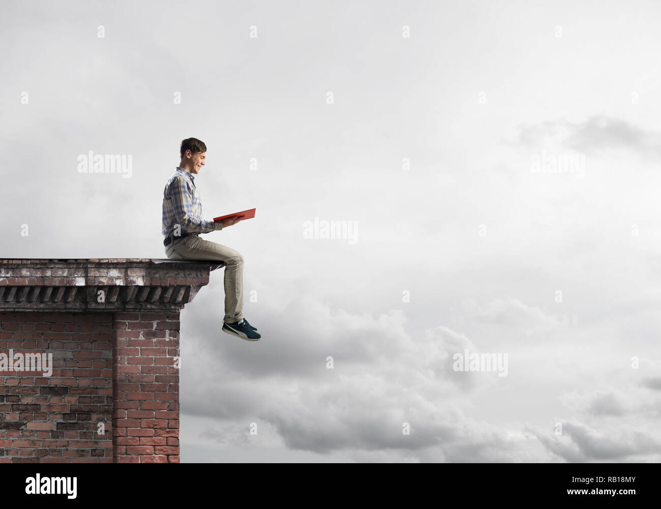 Man on roof edge reading book and cloudscape at background Stock Photo ...