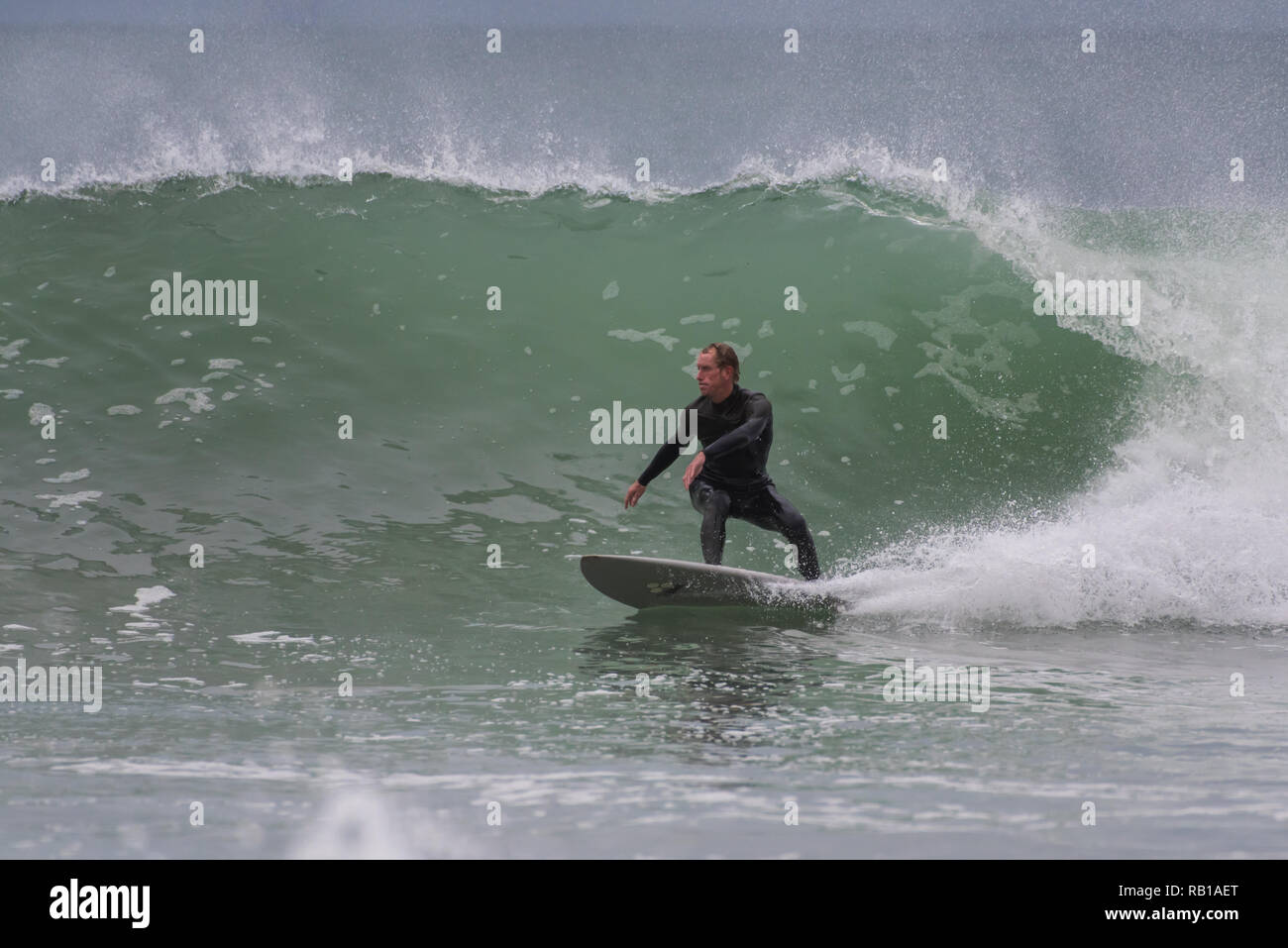 Skilled surfer in black wetsuit drops into a larger set wave and ...