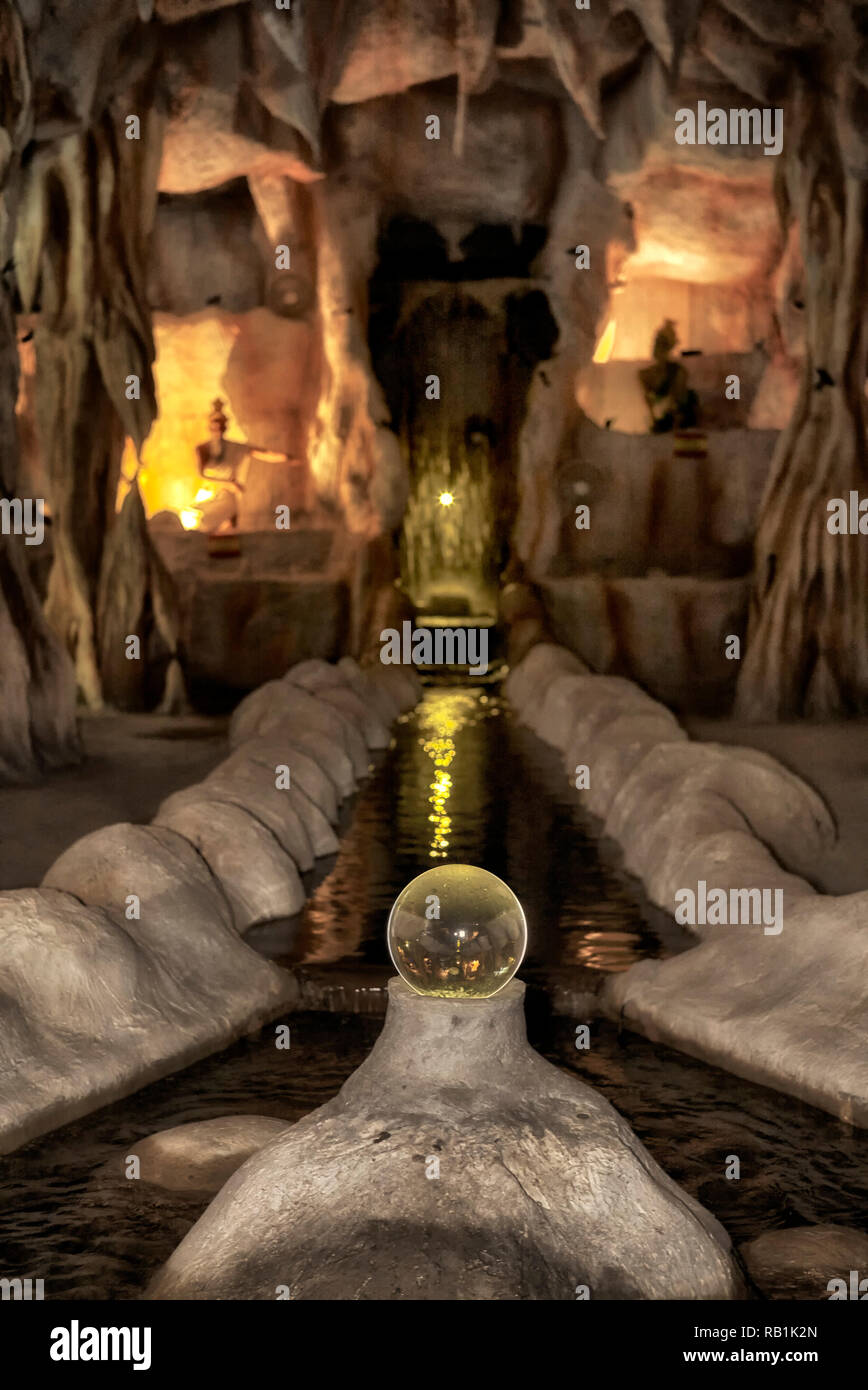 Thailand cave interior with illuminated statues and figures of hermits ...