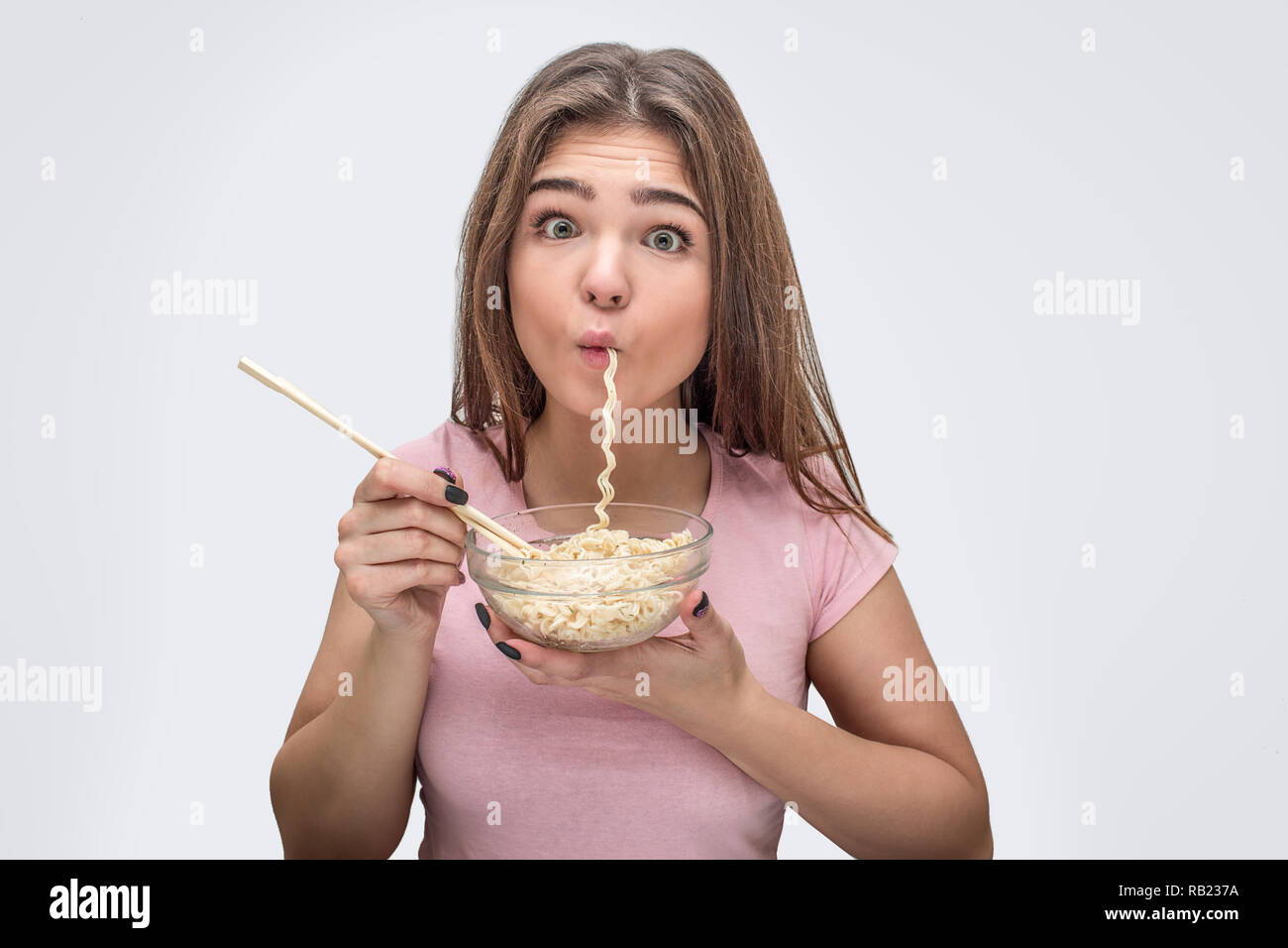 Funny young woman has some vermicelli in mouth. She eat it with ...