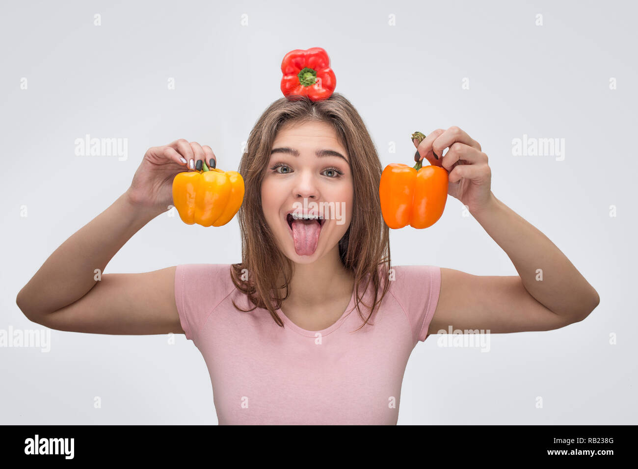Funny young woman look on camer and show tongue. She hold red peeper on ...
