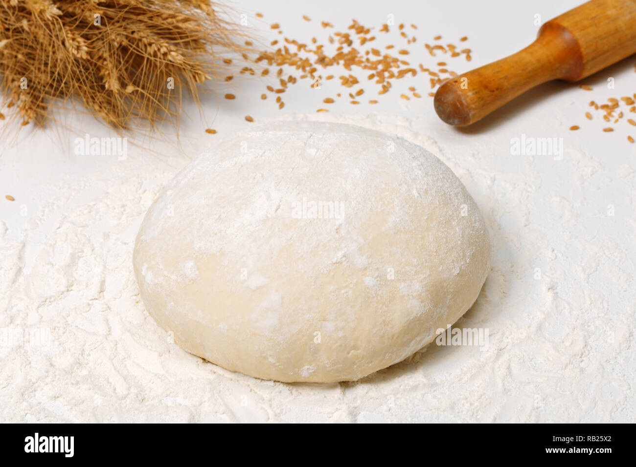 Raw fresh dough in the flour and ears of wheat on a white background ...