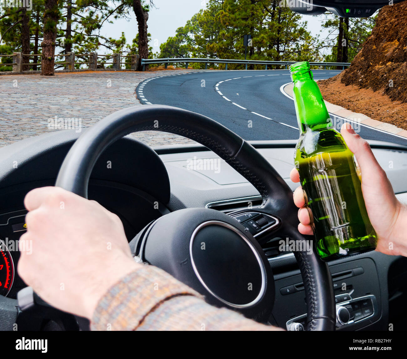 Drunk young man driving a car on the road with a bottle of beer. Don't ...