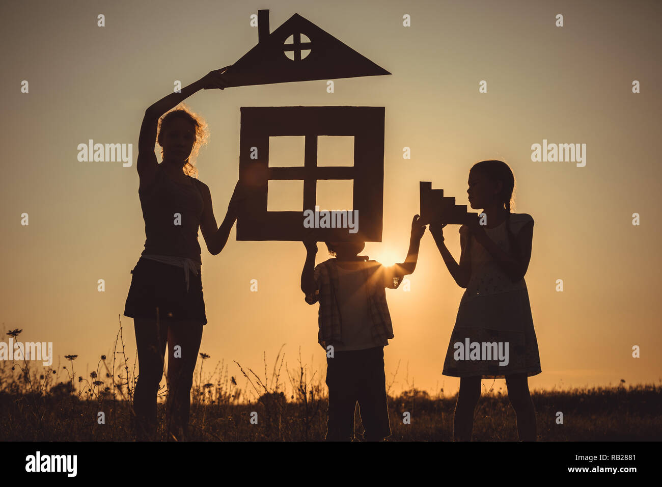 Happy children standing on the field at the sunset time. They build a ...