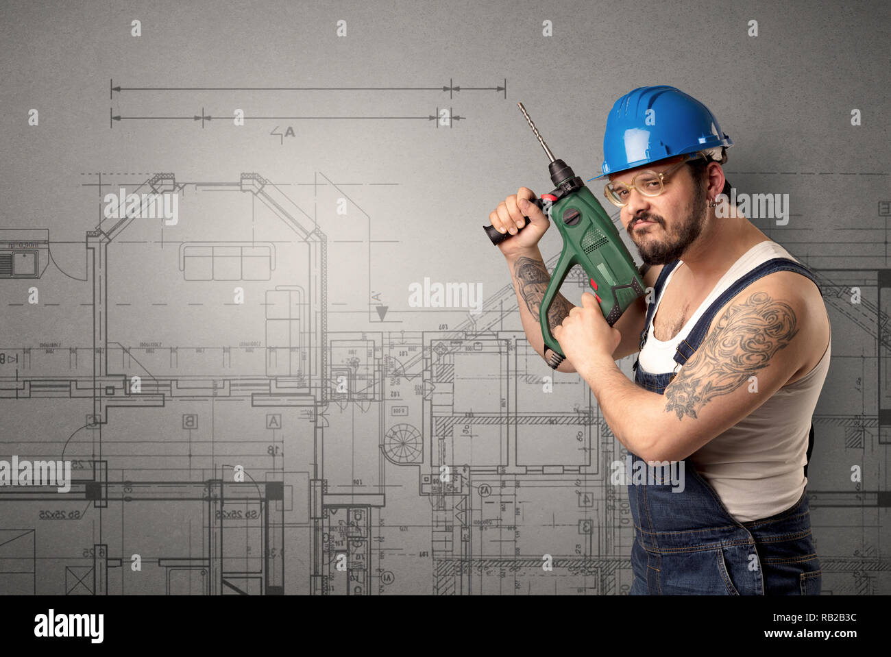 Worker standing with tool in his hand in front of technical drawings ...