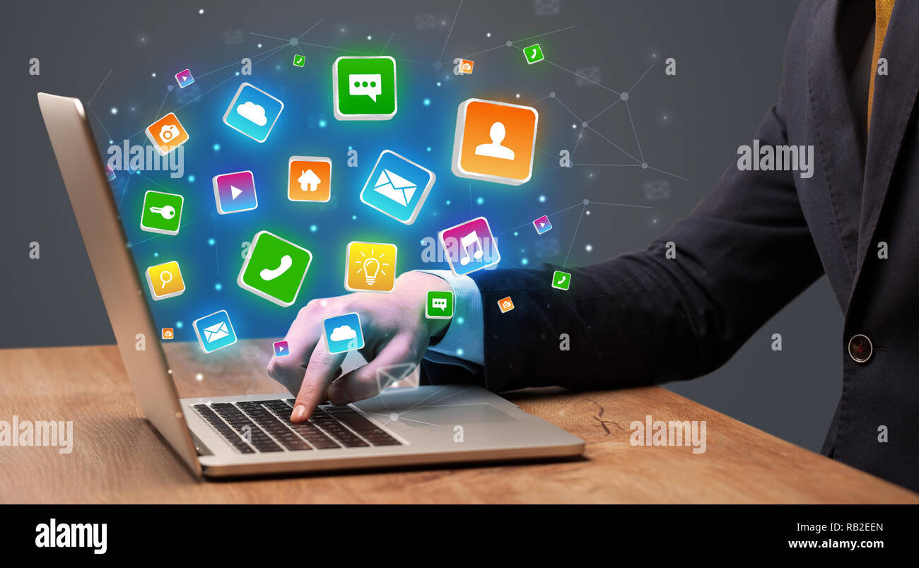 Businessman hand typing on laptop with flying application icons around ...
