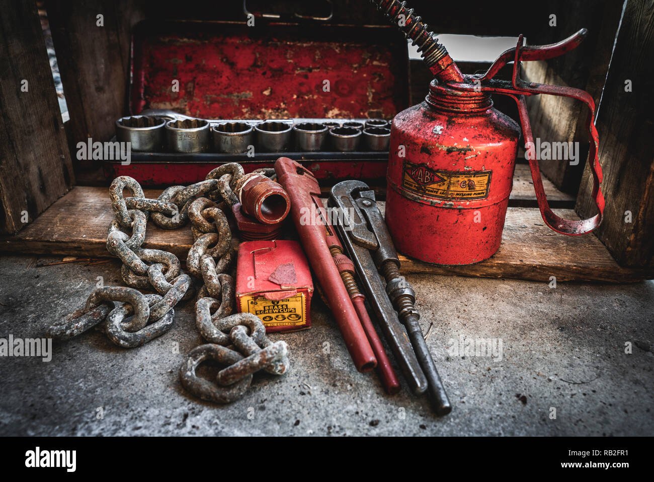 Old red vintage oil can with rusty chain and plumber tools on concrete ...