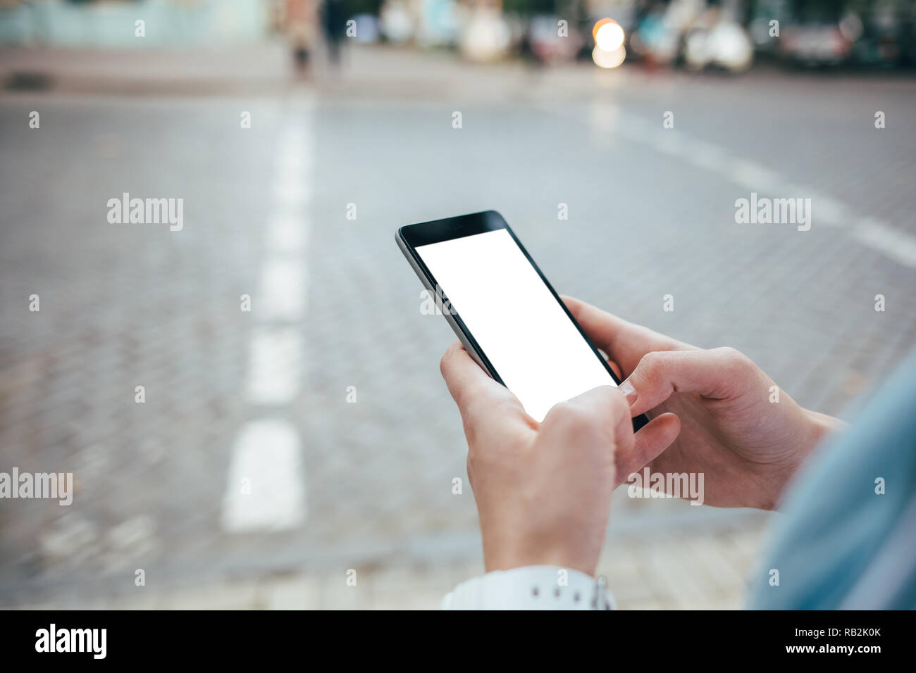 Woman's hands holding mobile phone with blank white screen in city ...