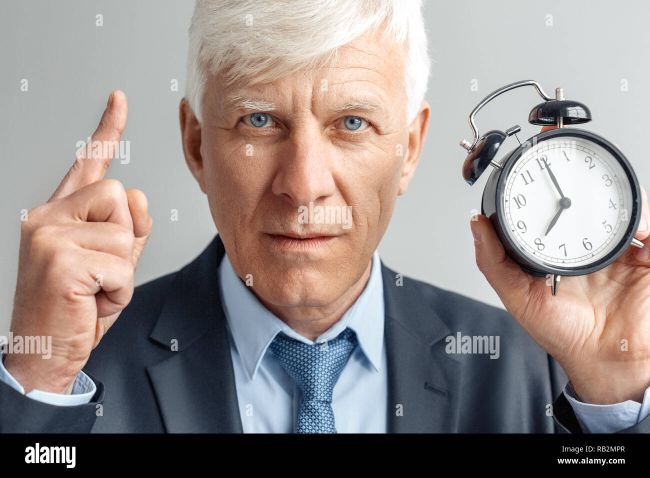 Senior business man studio standing isolated on gray wall holding alarm ...