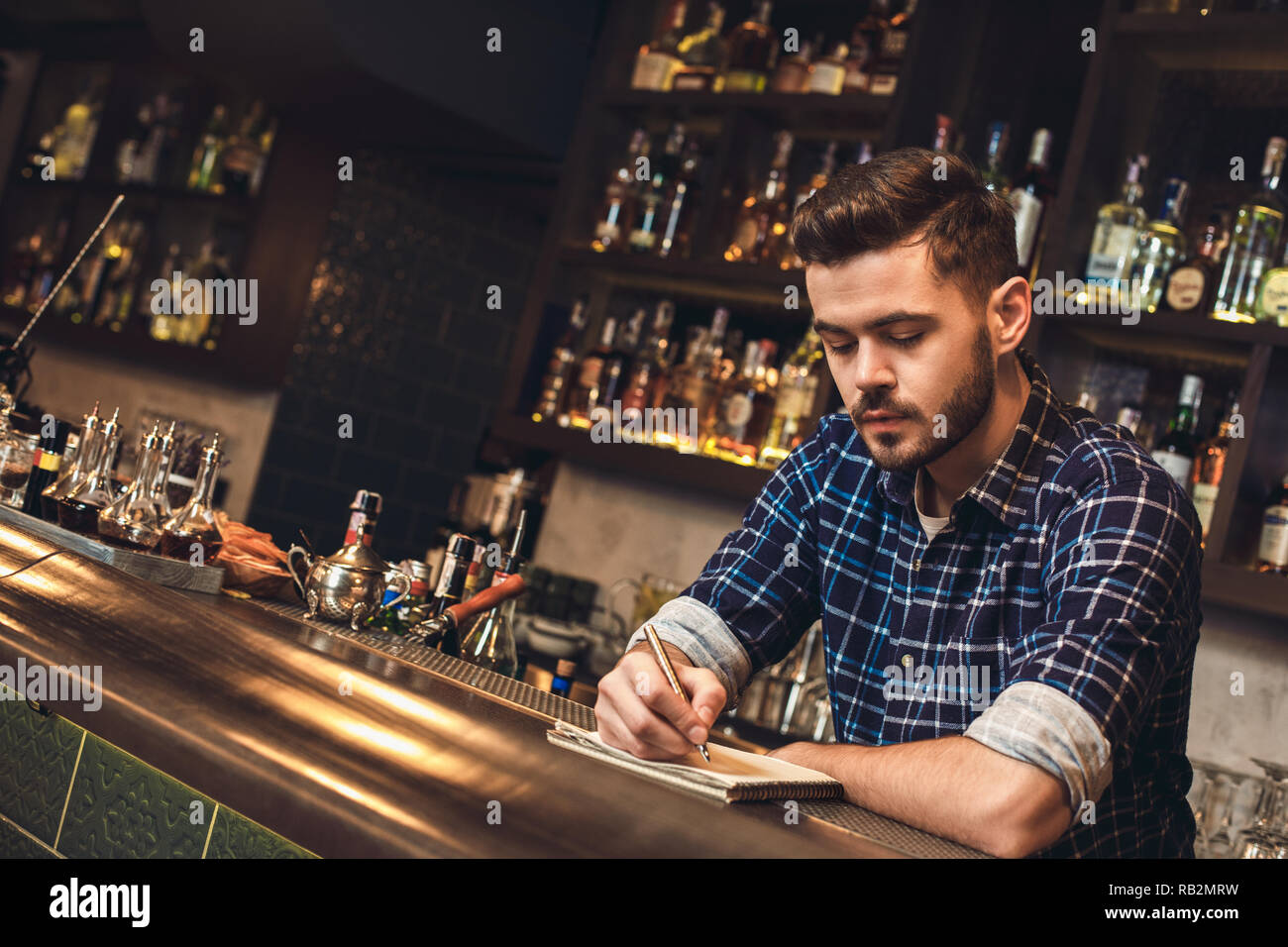 Young barman standing leaning on bar counter taking notes in planner ...
