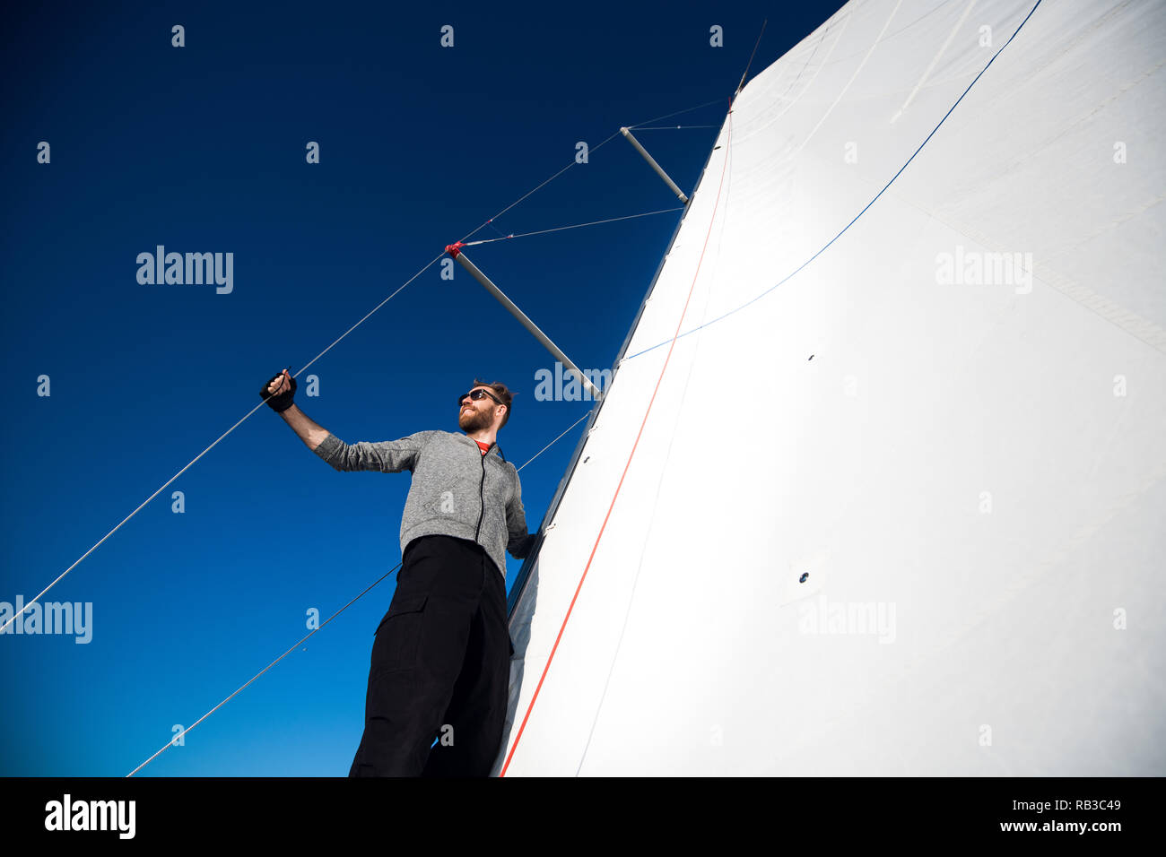 Yacht captain with a beard stands on sail boom on a sailing yacht ...
