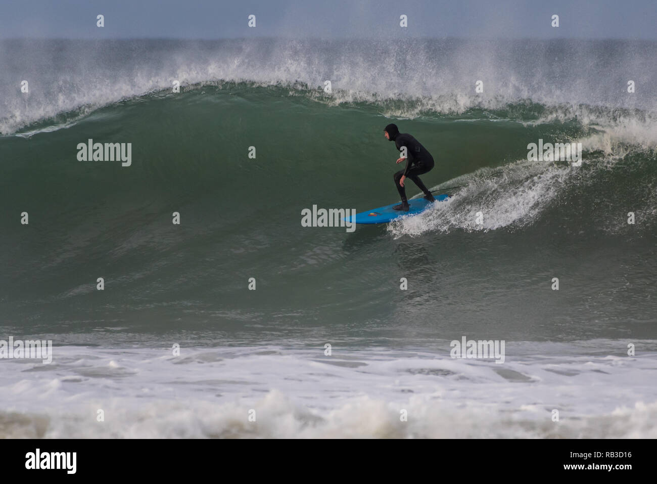 Brave hooded surfer tucking into the barrel of large set wave during ...