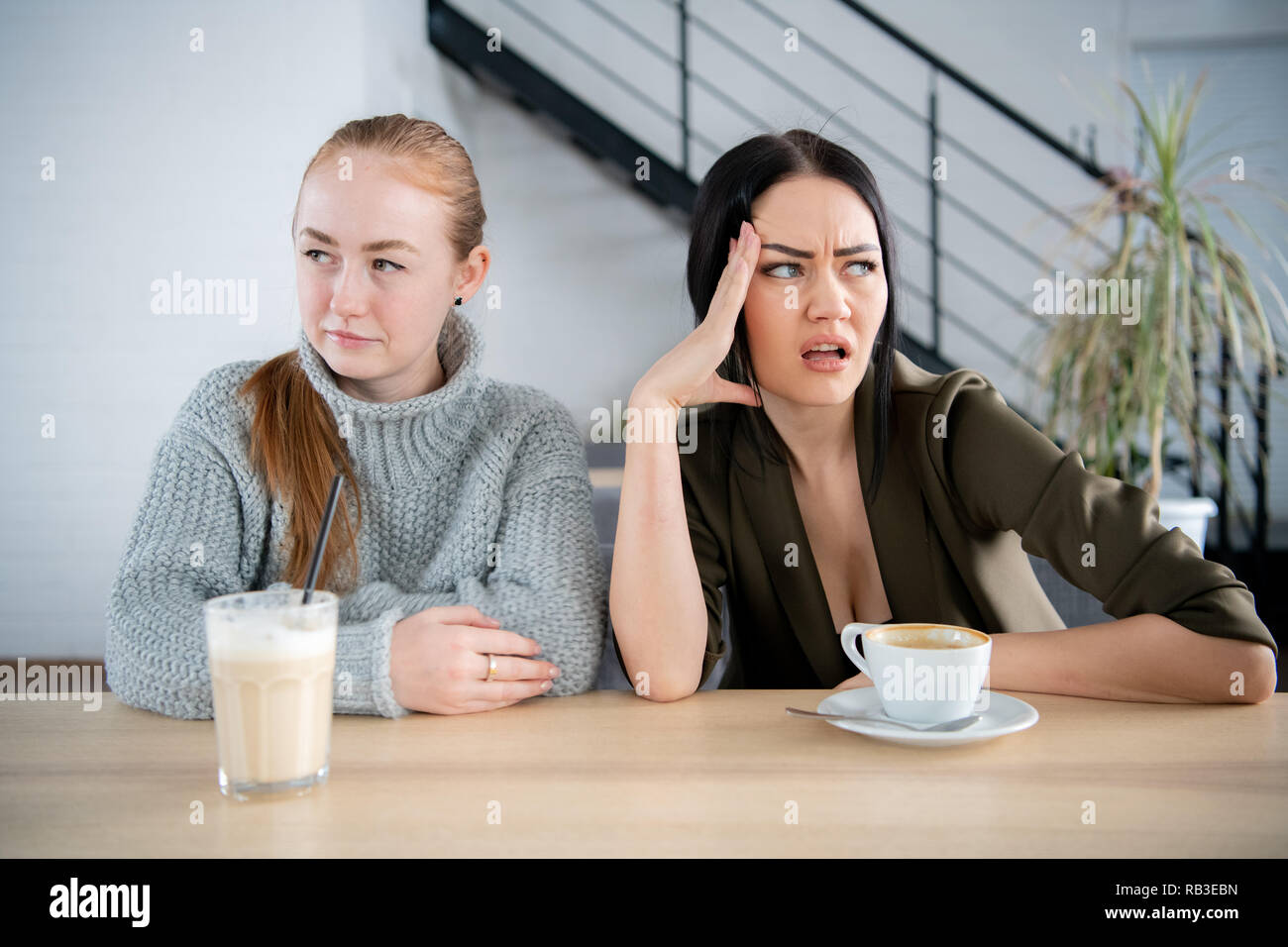 two girls young women sitting in a cafe with coffee cups, looking ...
