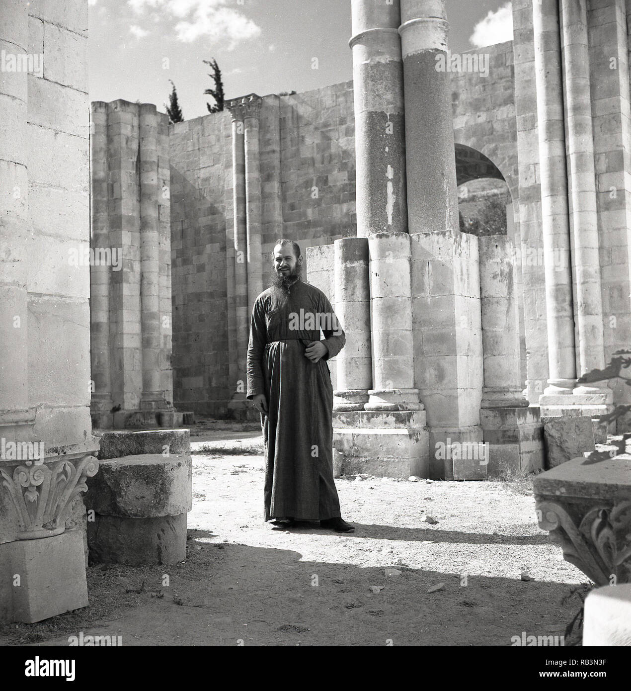 1950s, bearded Jordanian priest standing outside amongst the columned ...