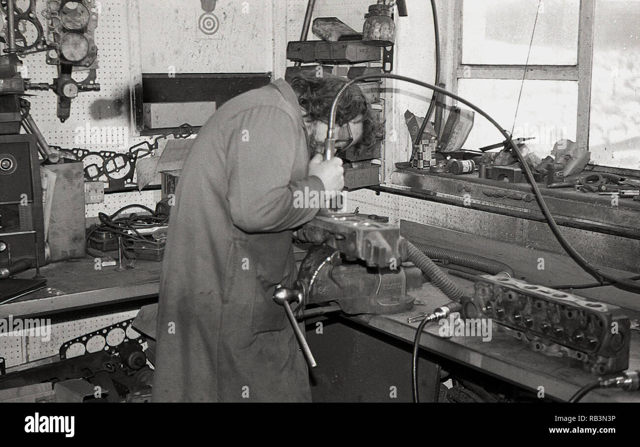 1970s, a male car mechanic in overalls in a garage workshop using a ...