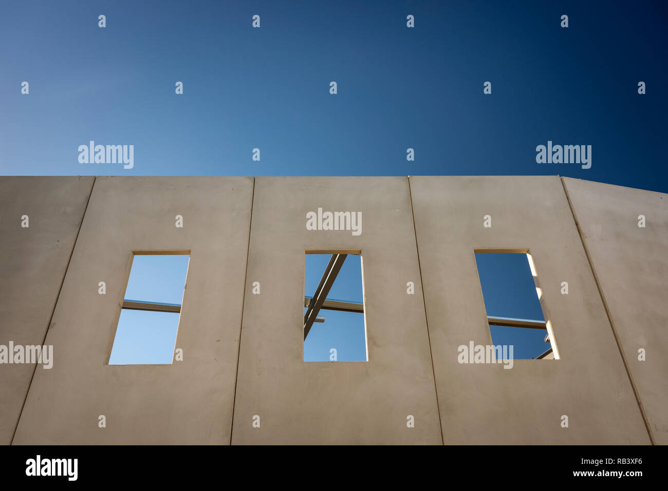Prefabricated concrete walls with windows, being erected against a blue ...