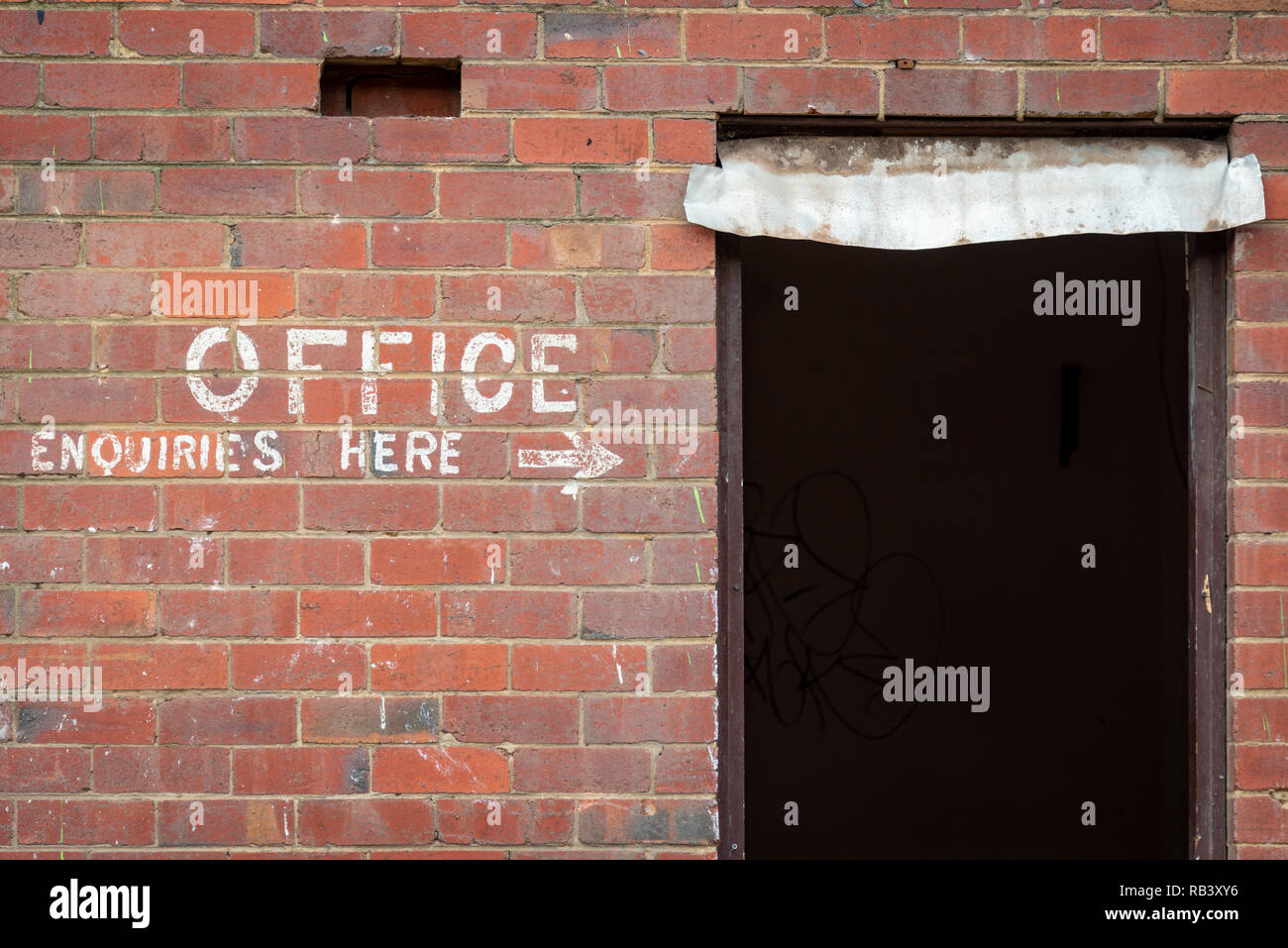 Old painted sign, Office Enquiries Here, on a red brick wall and an ...