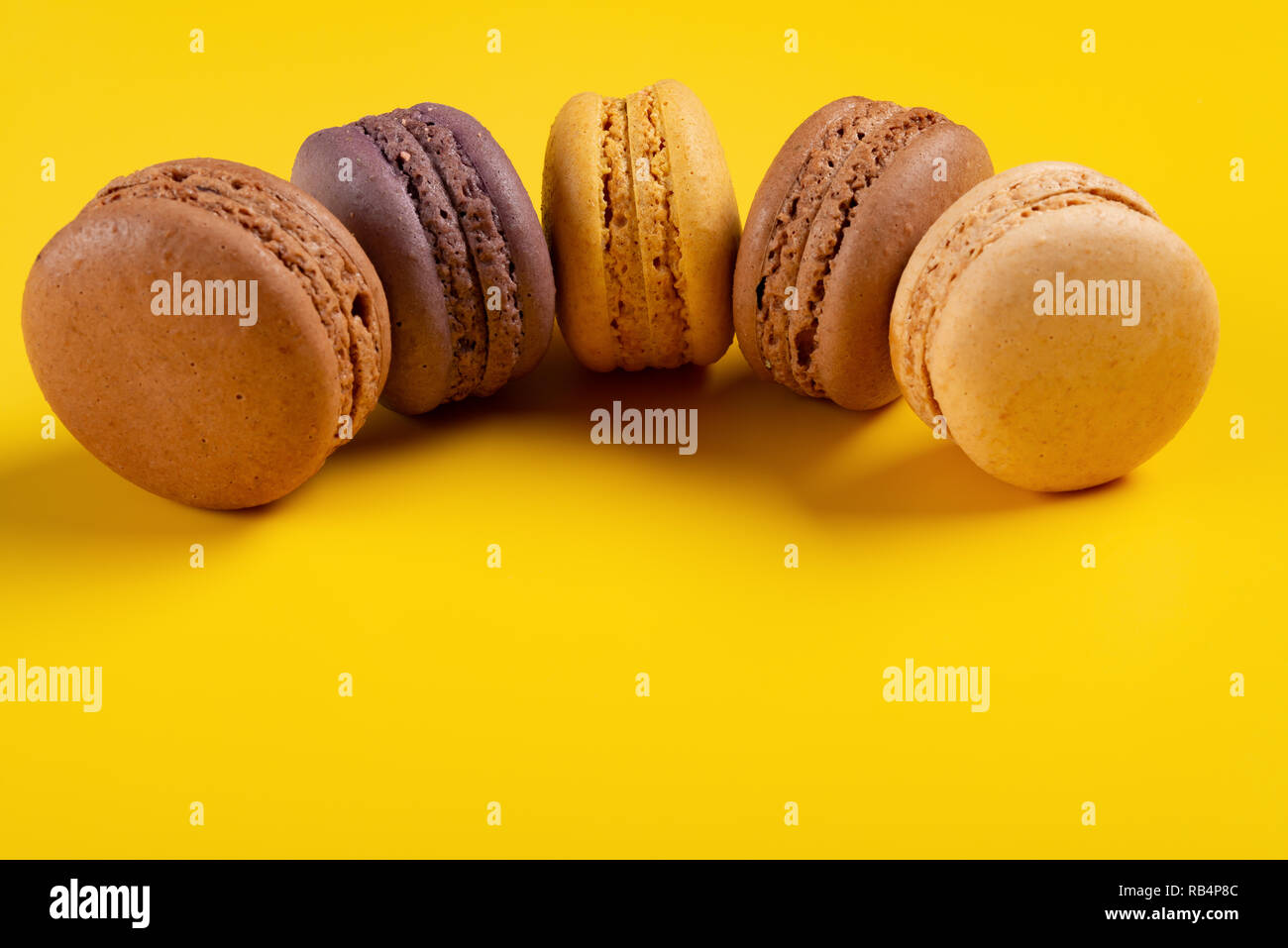 studio shoot of colorful macaroons line up curved on yellow background ...