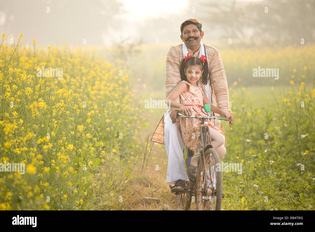 Happy farmer with his daughter riding bicycle on rapeseed agriculture ...