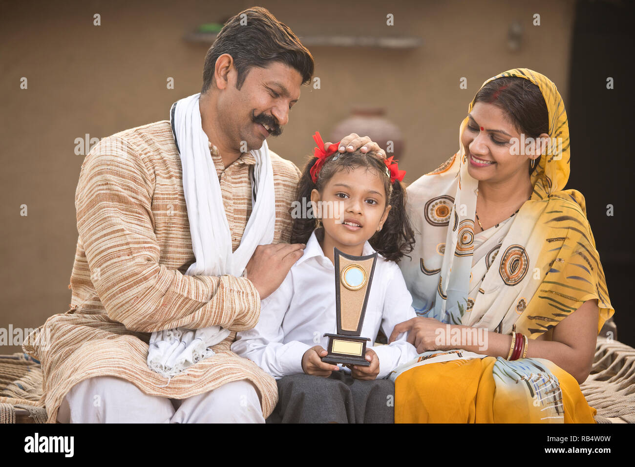 Proud Indian parents with little daughter holding trophy in school ...
