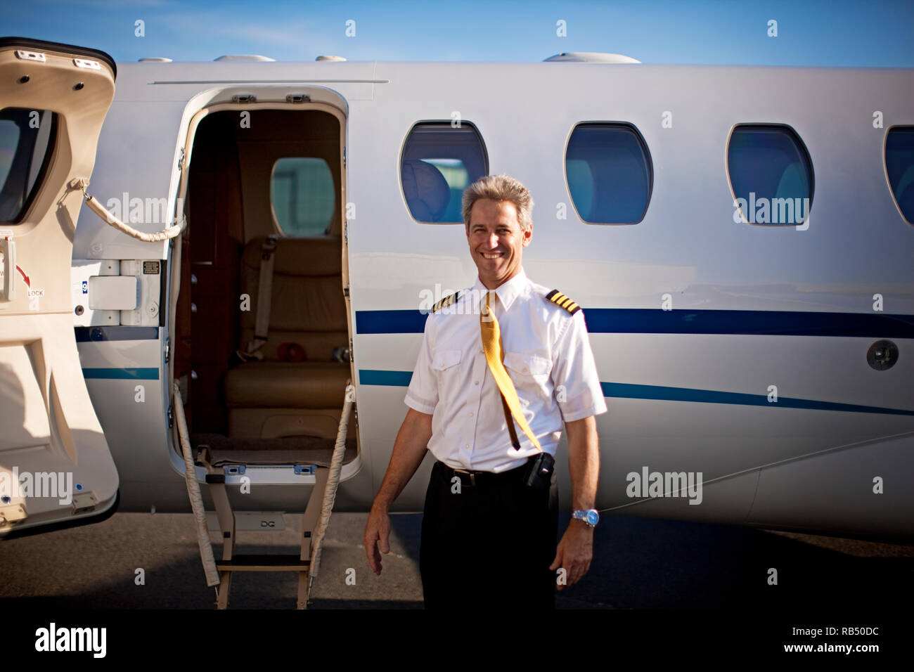 A pilot standing in front of a private jet and smiling Stock Photo - Alamy