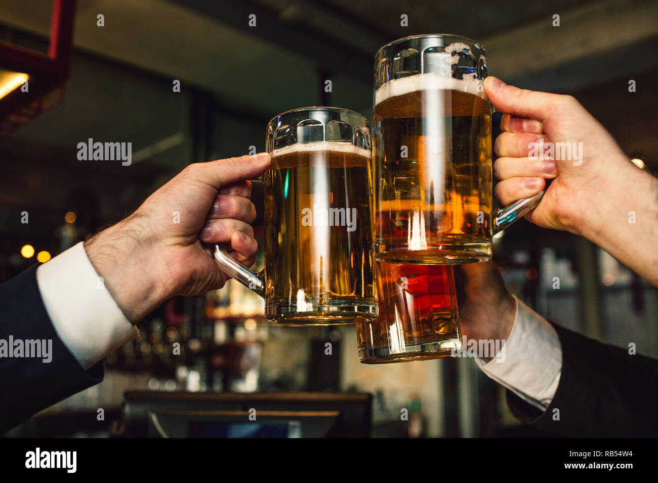 Picture of three mugs of beer in men hands. People wear suits. They are ...