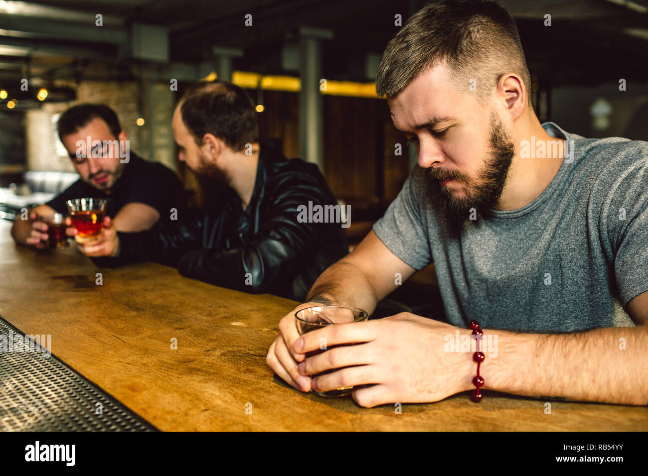 Young handsome man sit alone at bar counter. He look down. Other two ...