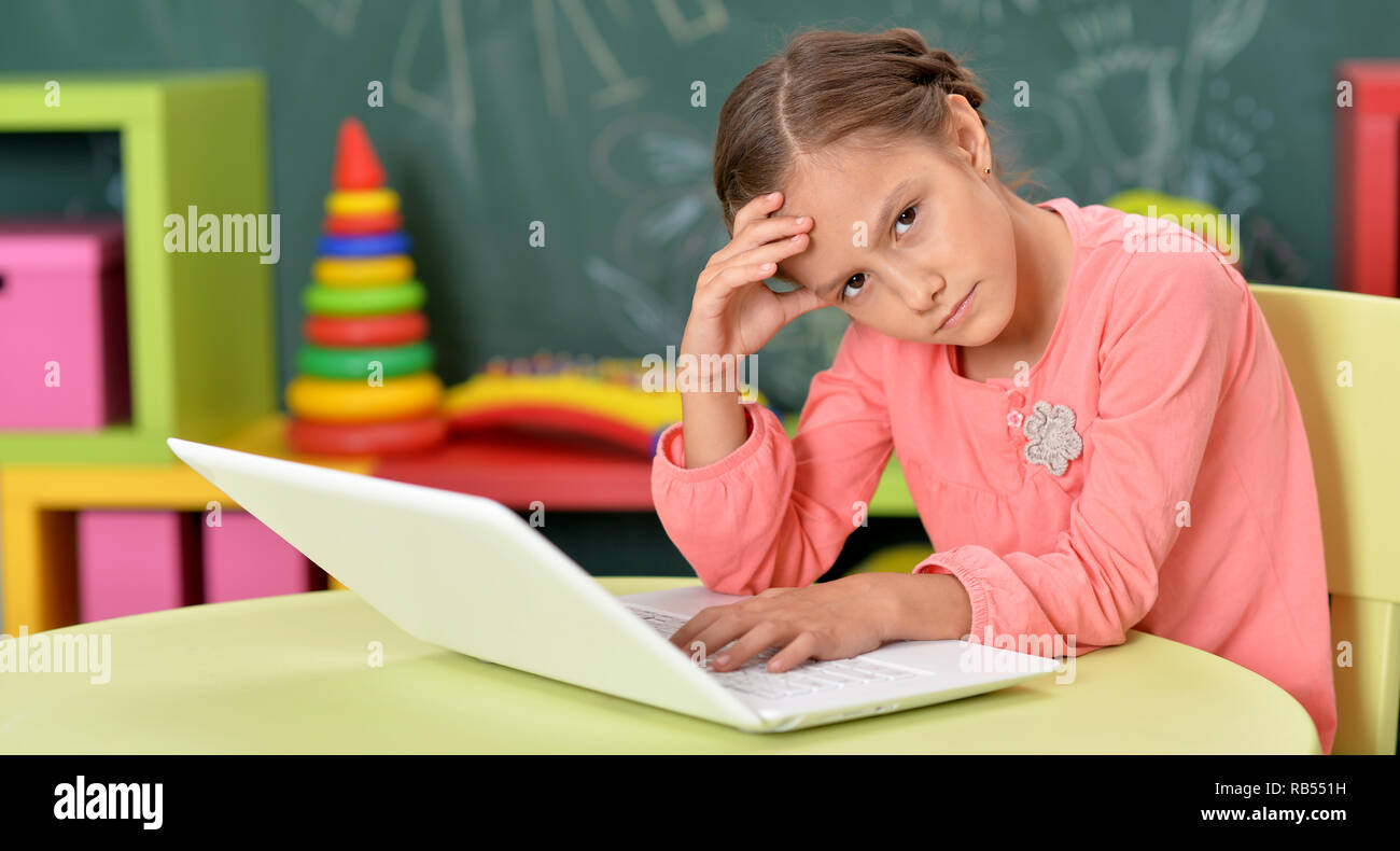 Little girl using laptop while sitting at desk in classroom Stock Photo ...