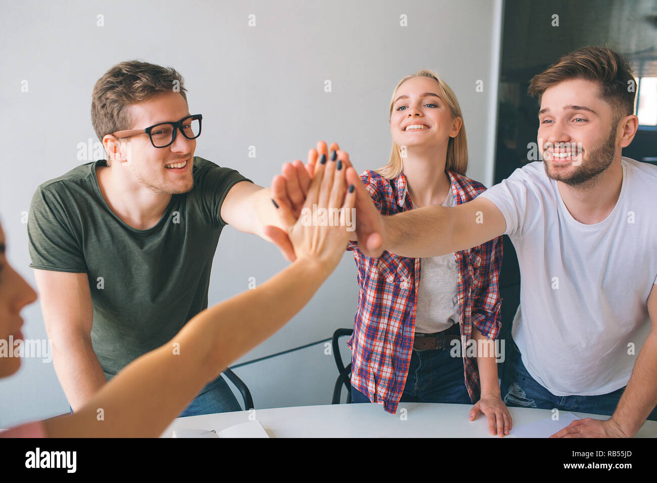 Four happy young people touch each other palms and joying. They stand ...