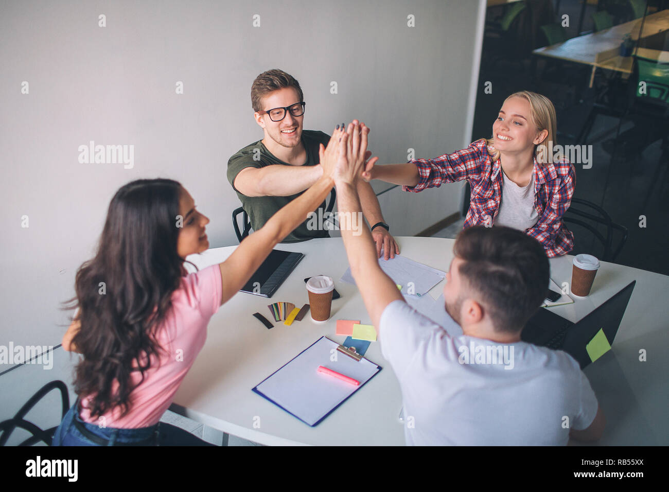Happy and cheerful young people sit around table and keep hands ...