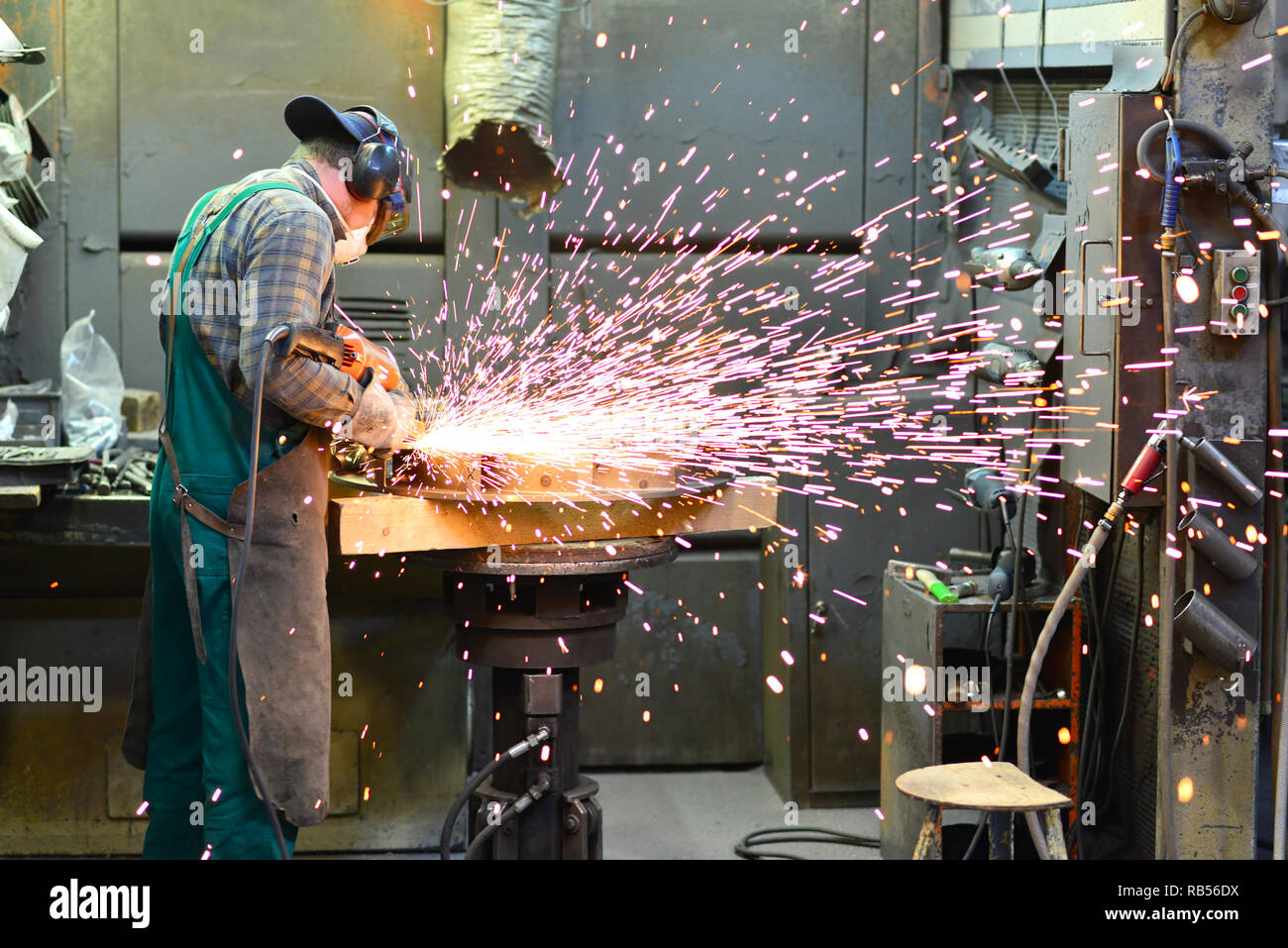 workers in safety clothing sanding a casting in an industrial company ...