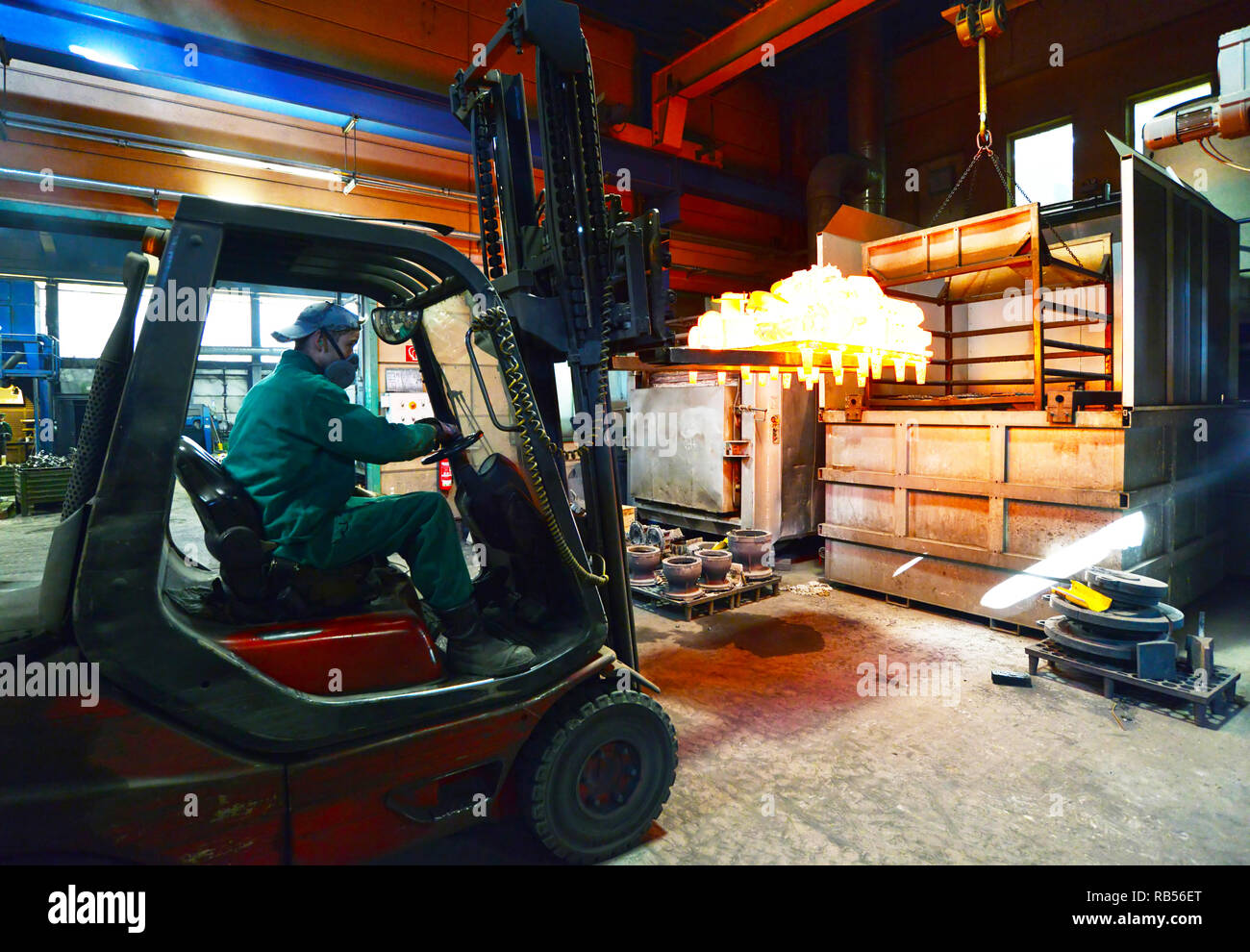 worker drives forklift to hardening blast furnace with glowing steel ...