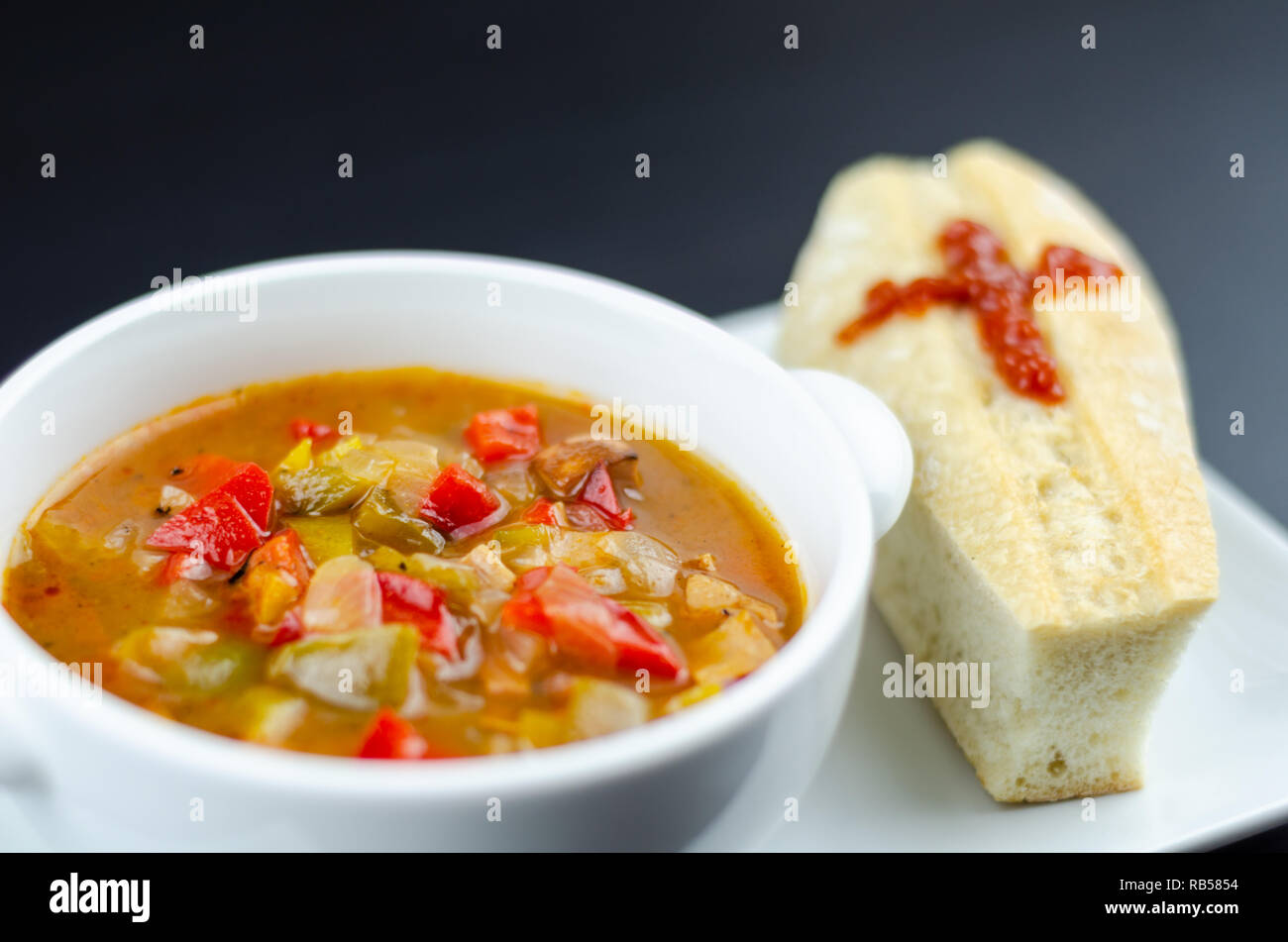 A delicious stew in a white ceramic bowl served with bread in the shape ...
