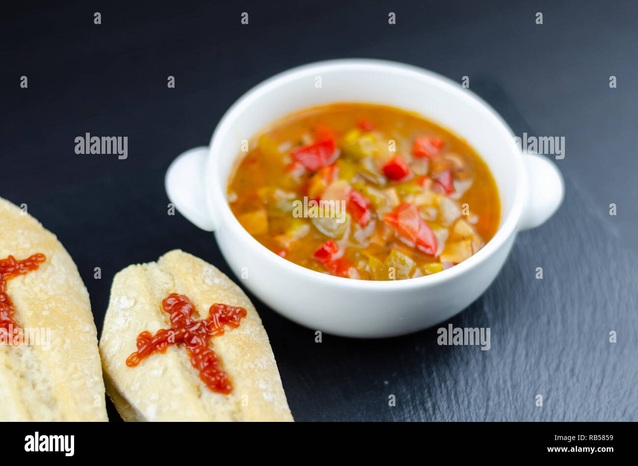 A delicious stew in a white ceramic bowl served with bread in the shape ...