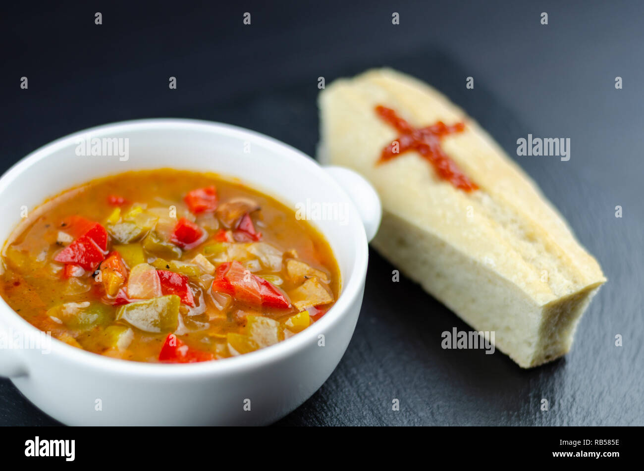 A delicious stew in a white ceramic bowl served with bread in the shape ...