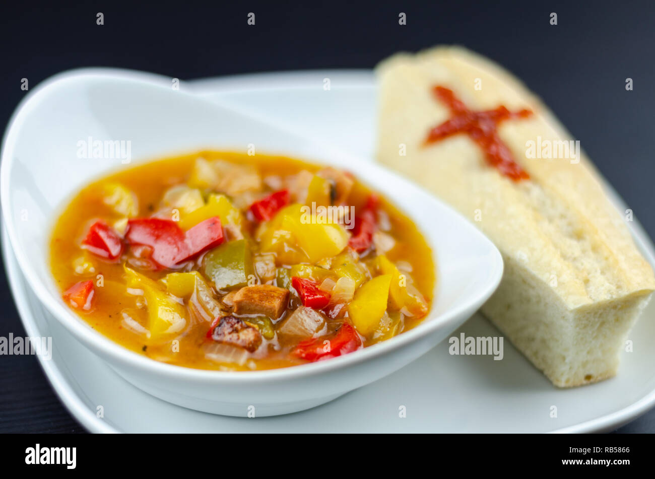 A delicious stew in a white ceramic bowl served with bread in the shape ...